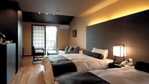 Quarto de hotel com duas camas, uma escrivaninha, uma cadeira, um abajur e vista para o exterior.