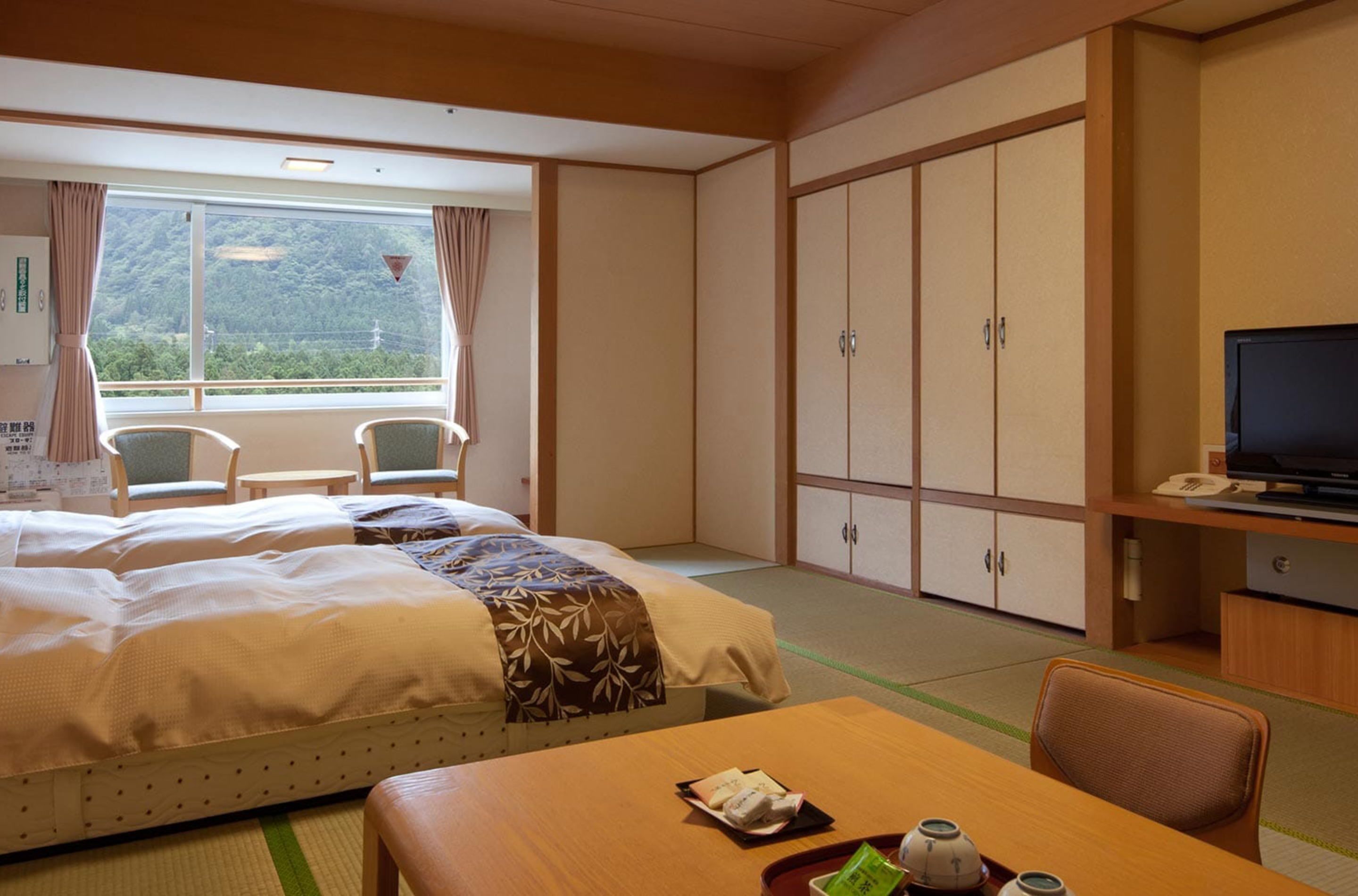 Quarto de hotel com duas camas, uma mesa de jantar, uma televisão e vista para uma paisagem montanhosa.
