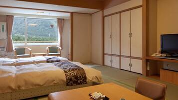 Quarto de hotel com duas camas, uma mesa de jantar, uma televisão e vista para uma paisagem montanhosa.