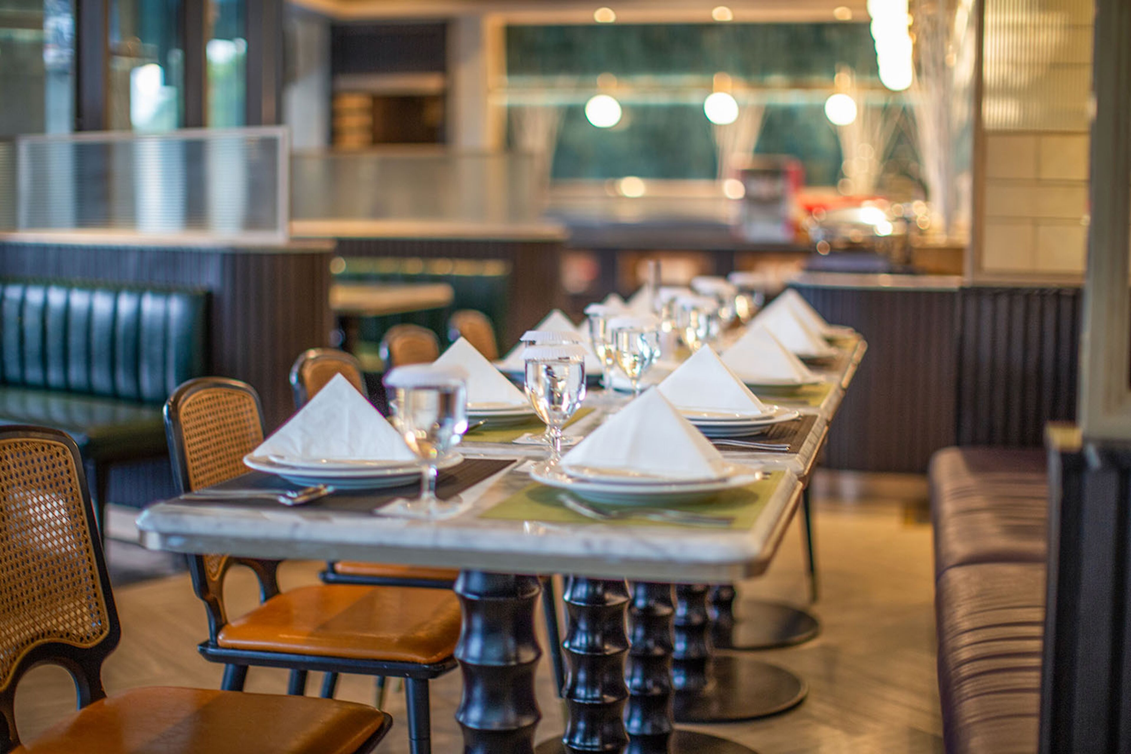Um restaurante com uma mesa de jantar comprida posta para uma refeição, rodeado por cadeiras e assentos acolchoados.