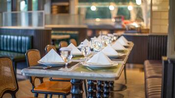 Um restaurante com uma mesa de jantar comprida posta para uma refeição, rodeado por cadeiras e assentos acolchoados.