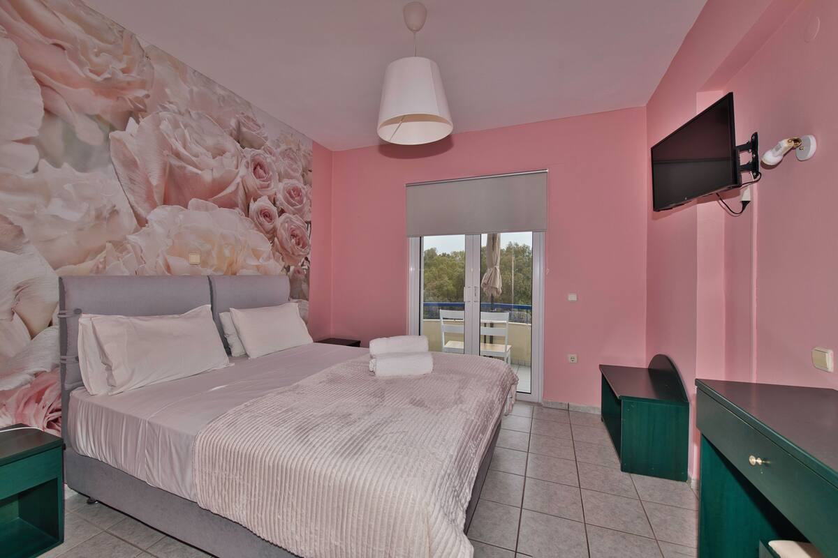 Quarto com cama, televisão, escrivaninha e porta para varanda.