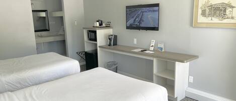 Quarto de hotel com duas camas, uma mesa de escritório com computador, televisão e uma pequena cozinha.