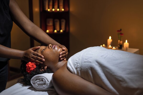 Uma pessoa recebendo uma massagem em um quarto com velas e uma estante de livros ao fundo.