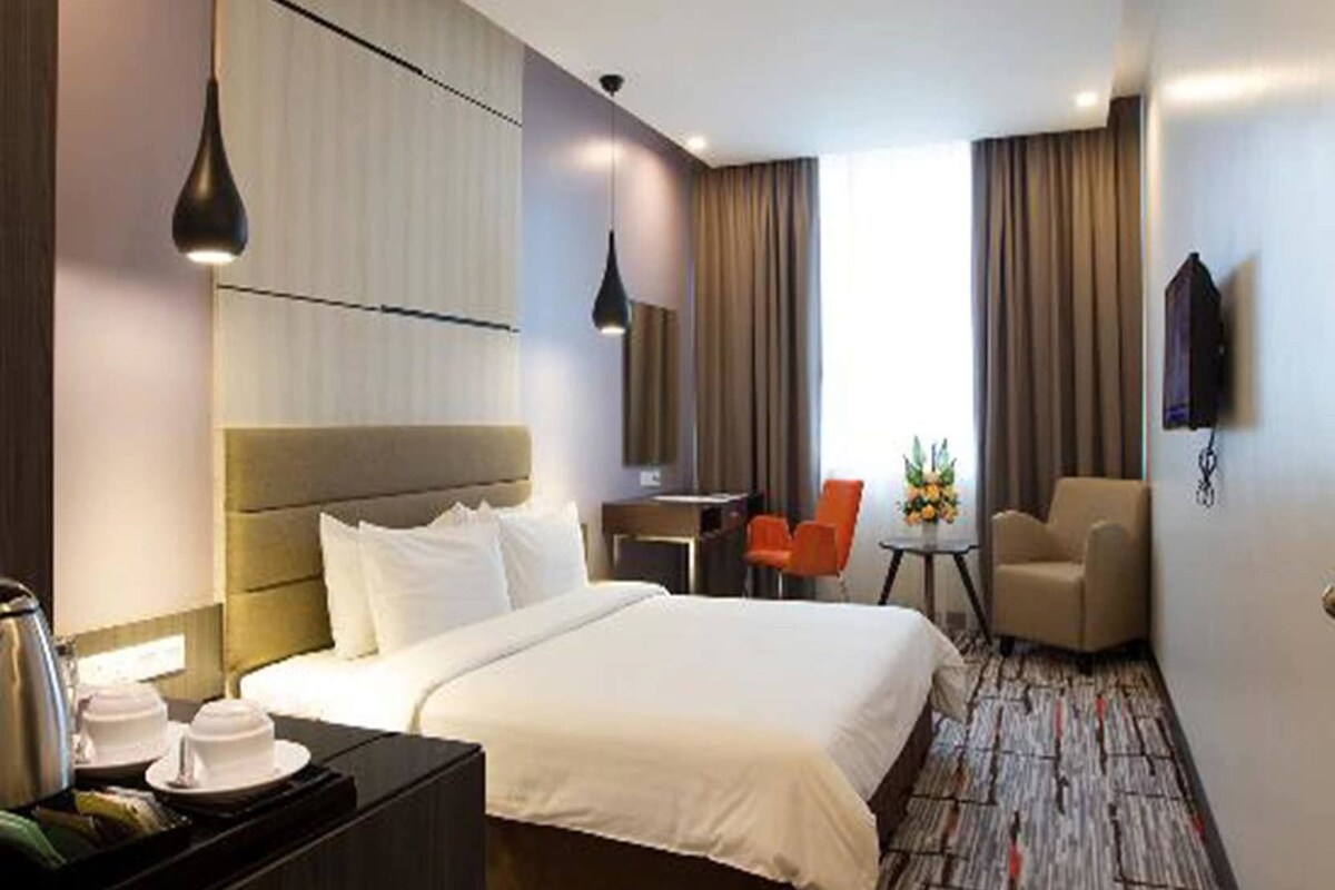 Quarto de hotel com cama, escrivaninha, duas cadeiras, cafeteira e televisão.