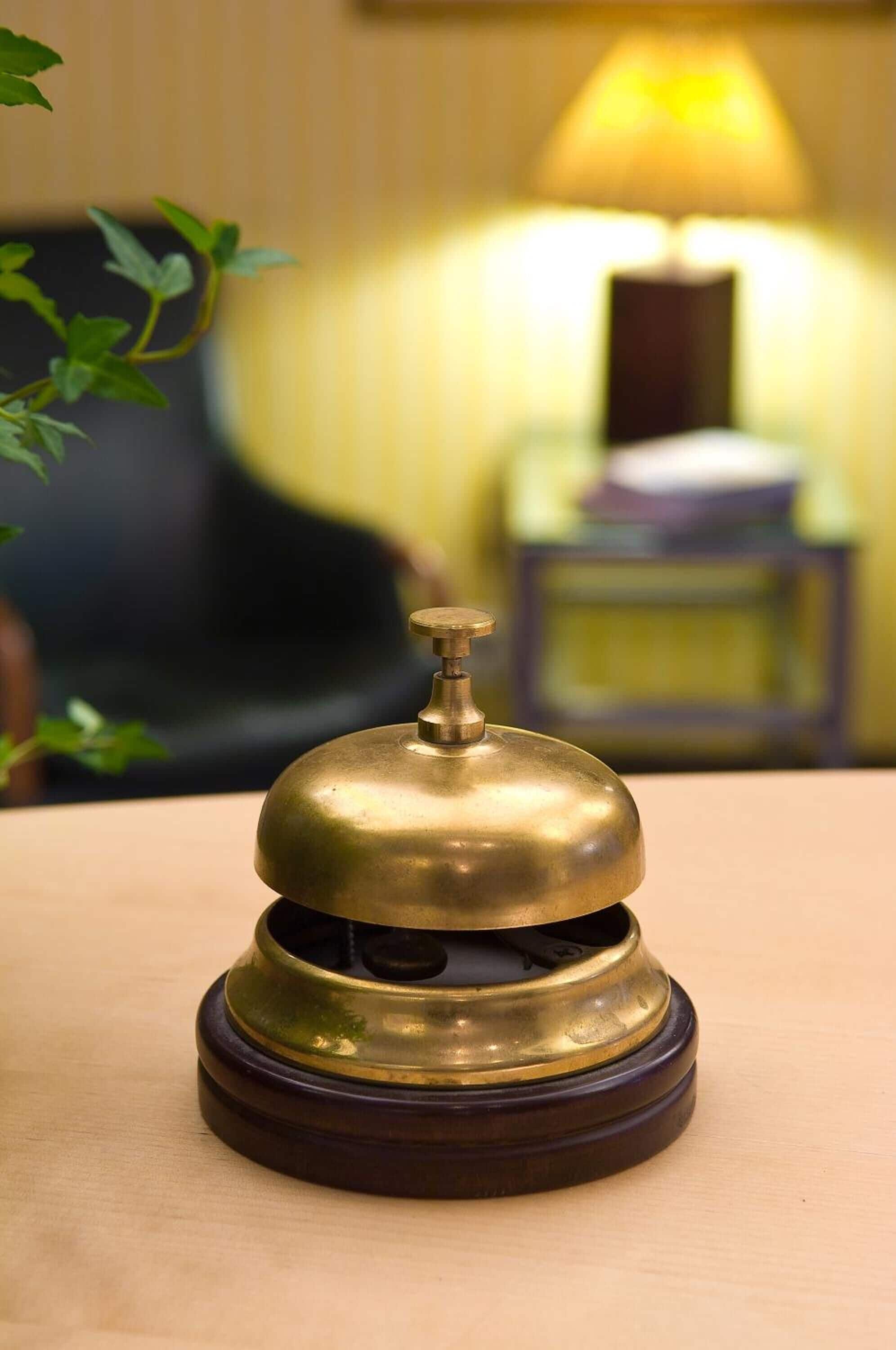 Um sino de latão sobre uma base de madeira, provavelmente usado para solicitar o serviço de quarto ou atendimento em um hotel.