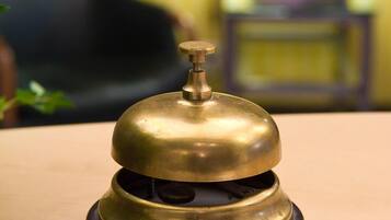 Um sino de latão sobre uma base de madeira, provavelmente usado para solicitar o serviço de quarto ou atendimento em um hotel.