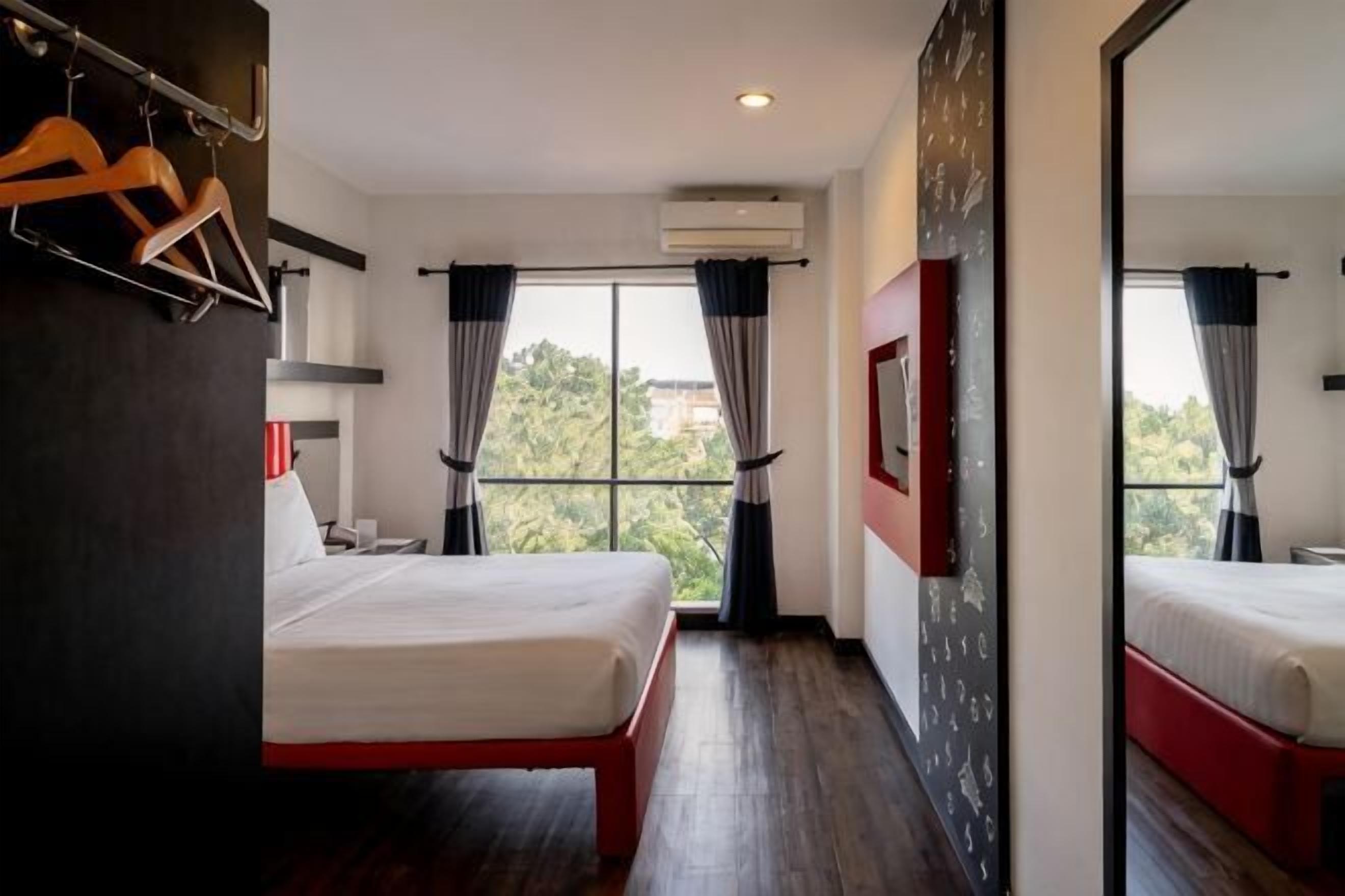 Quarto de hotel com duas camas, uma janela grande e vista para árvores.