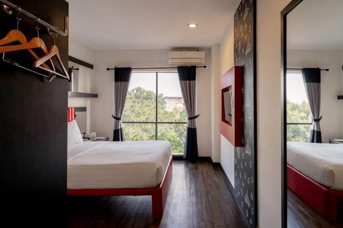 Quarto de hotel com duas camas, uma janela grande e vista para árvores.