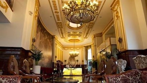 Um hall luxuoso com lustres ornamentados, móveis elegantes e um balcão de recepção imponente.