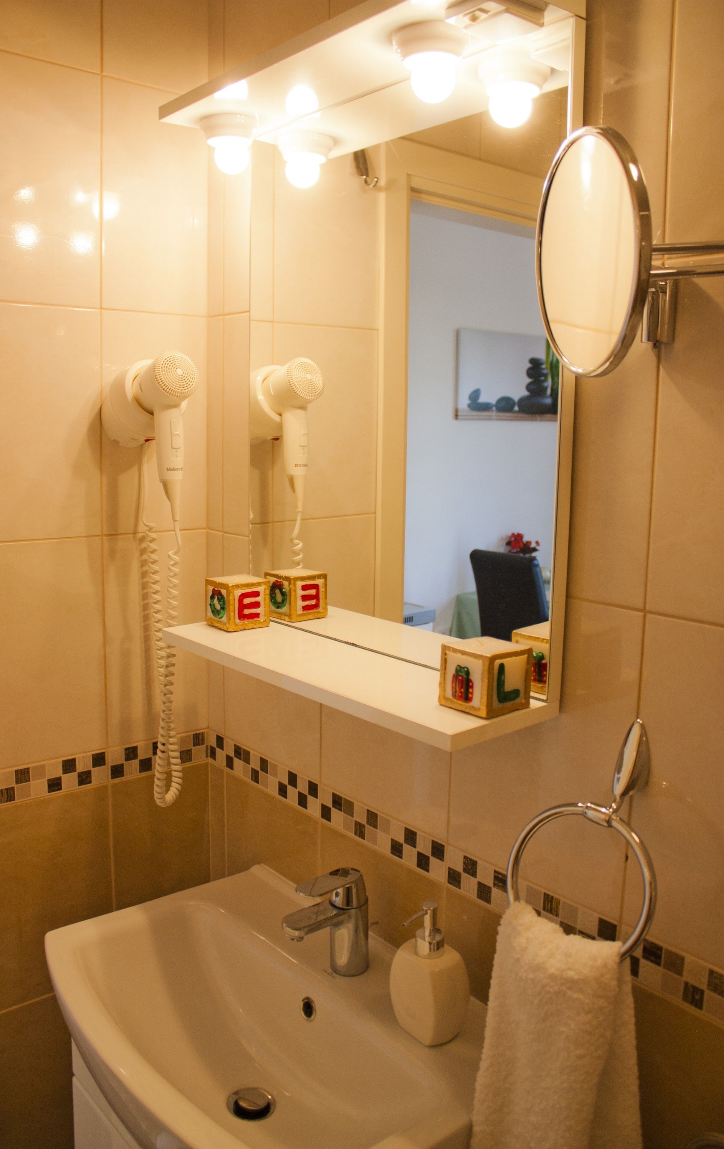 Casa de banho com lavatório, espelho e dois secadores de cabelo fixados na parede.