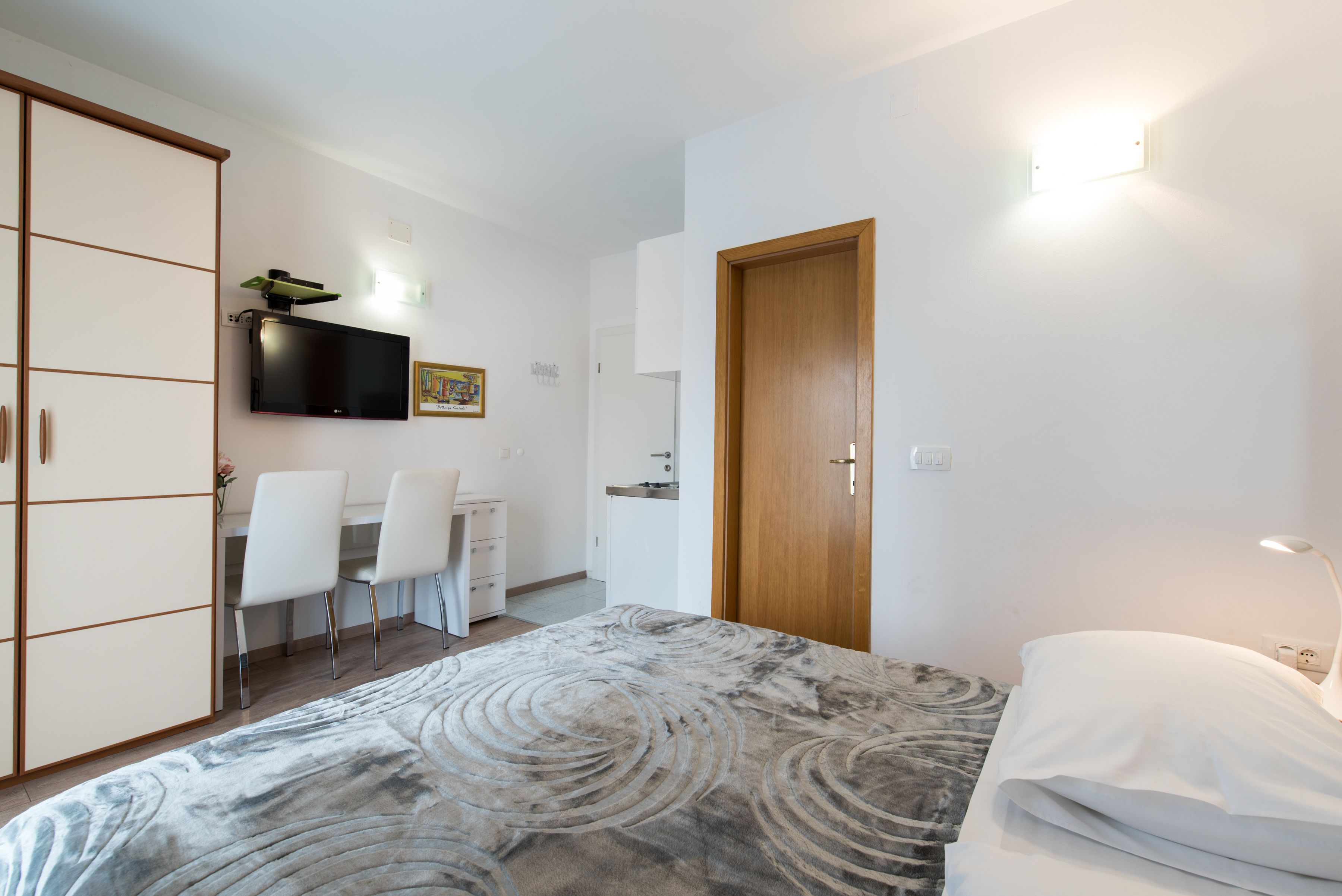 Quarto com cama, escrivaninha, cadeiras, televisão e guarda-roupa.