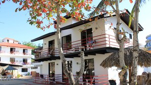 Um edifício de dois andares com varandas, área de estar ao ar livre e estrutura de telhado de palha.
