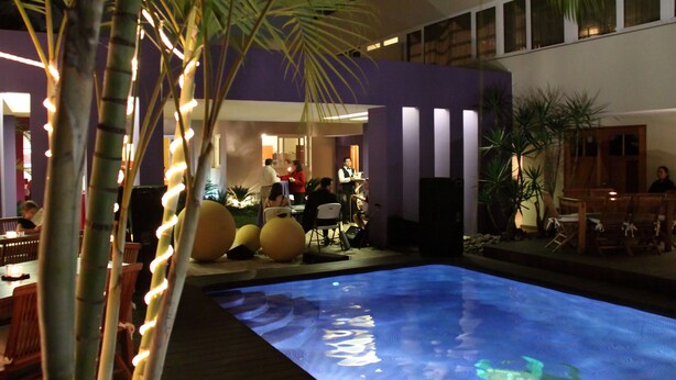 Piscina interna com superfície de água azul límpida, cercada por plantas de bambu e áreas de estar.