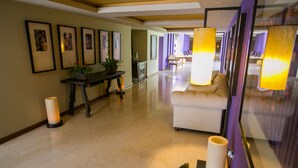 Um saguão de hotel com obras de arte emolduradas nas paredes, um balcão de recepção, um sofá e uma luminária grande.