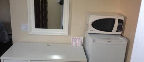 Uma cozinha compacta com bancada branca, micro-ondas e geladeira.