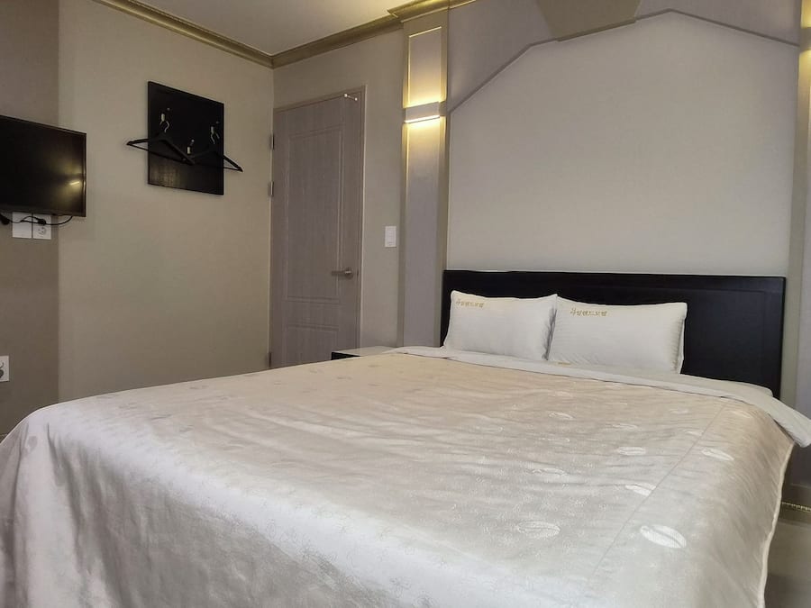 Quarto de hotel com cama, televisão de tela plana na parede, pequena área de kitchenette com chaleira e uma porta.