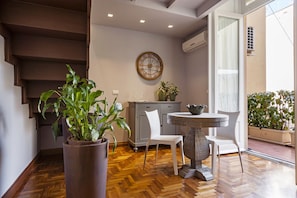 Um interior moderno com escada, área de jantar com mesa redonda, planta em vaso, cadeira branca e relógio na parede.