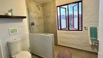Casa de banho com sanita, chuveiro e janela com vista para as montanhas.