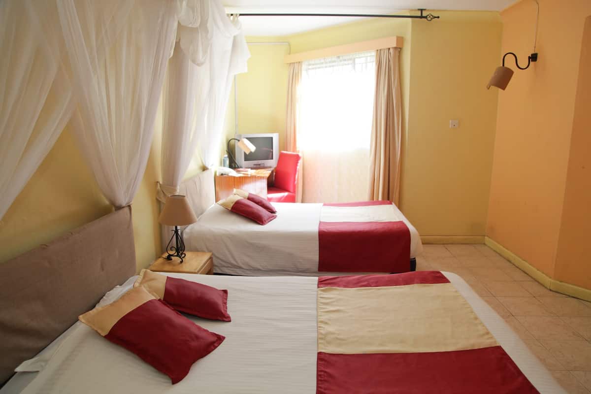 Quarto de hotel com duas camas, uma escrivaninha com computador, uma cadeira e uma janela com cortinas.