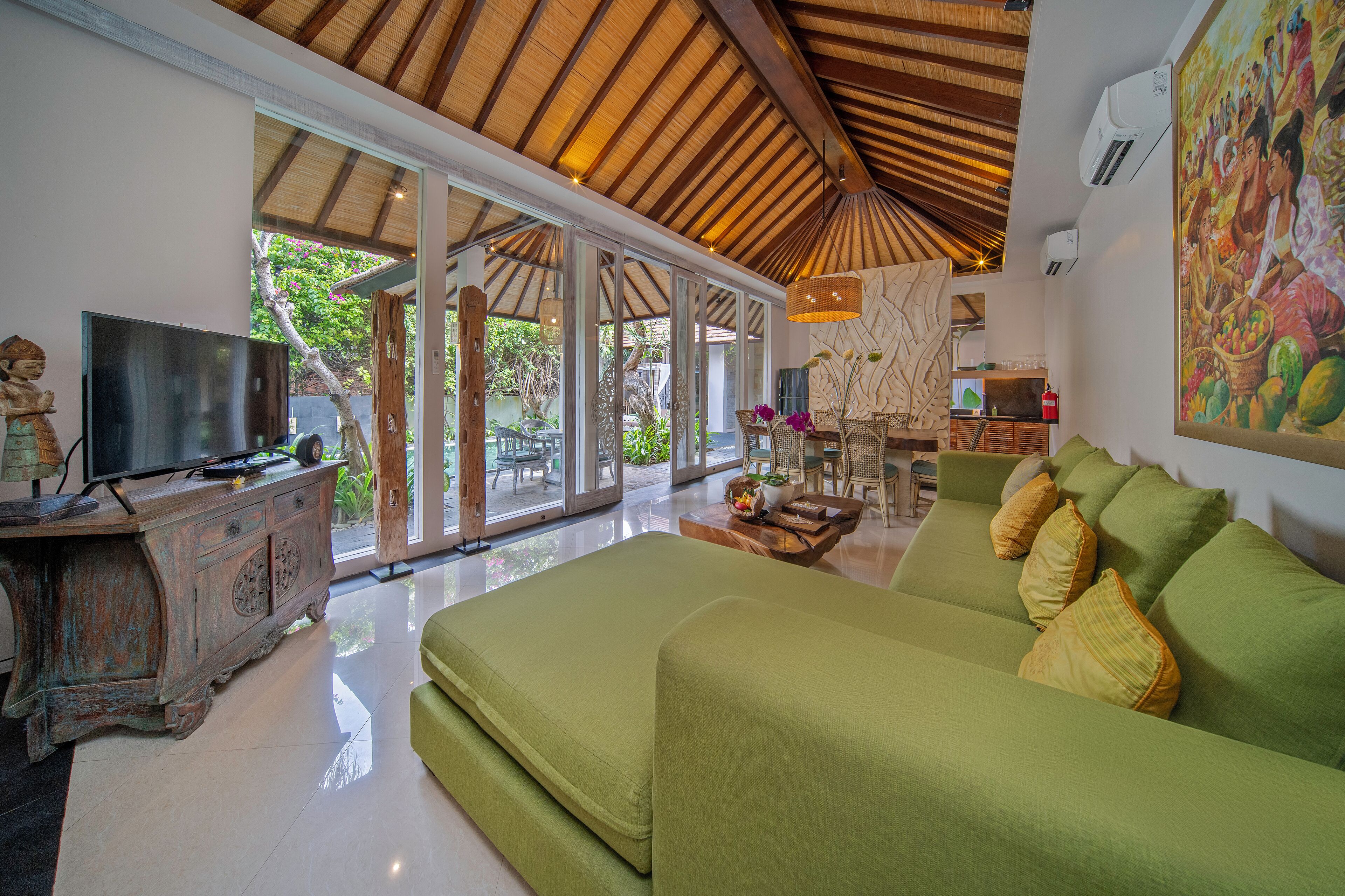 Uma sala de estar ampla com um sofá verde, teto de madeira e uma televisão sobre um armário de madeira.