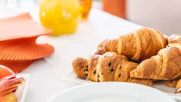 Mesa de café da manhã com croissants em um prato branco, um vaso amarelo e guardanapos laranja.