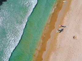 Vista aérea de uma praia com águas turquesa cristalinas e areal arenoso.