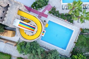 Uma piscina com escorregador amarelo, rodeada por um muro de pedra e vegetação.