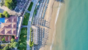 Vista aérea de um hotel à beira-mar, com fileiras de guarda-sóis, um estacionamento e um edifício com um padrão de telhado característico.
