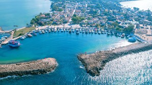Vista aérea de uma cidade costeira com um porto de iates, molhes rochosos e edifícios residenciais.
