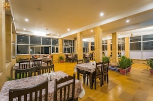 Uma ampla área de refeições interna com várias mesas e cadeiras, grandes janelas e ventiladores de teto.