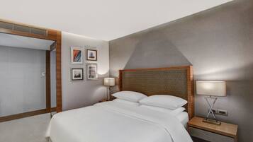Quarto de hotel com uma cama grande, mesa de cabeceira com abajur, televisão fixada na parede e quadros decorativos.