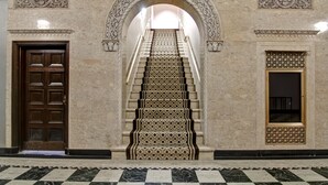Uma escadaria de mármore com desenhos elaborados, ladeada por portais ornamentados e um piso com padrão.