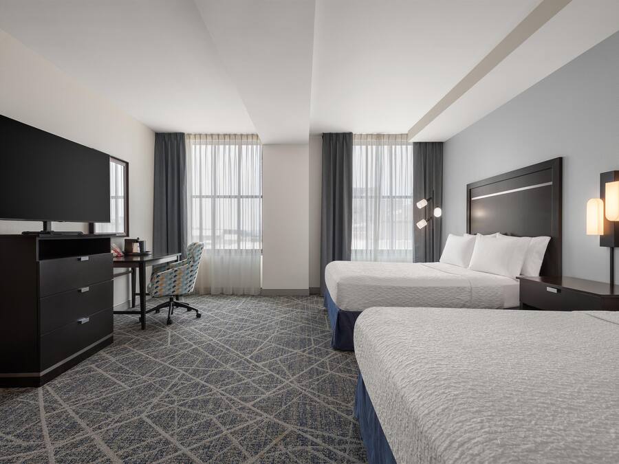 Quarto de hotel com televisão de tela plana, escrivaninha, duas camas e carpete estampado.