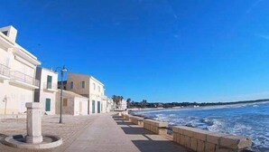 Um calçadão costeiro com edifícios, céu claro e o mar.