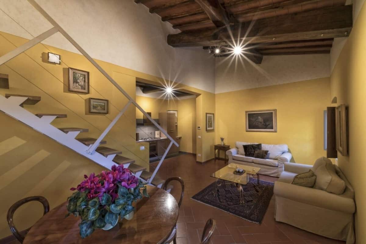 Uma sala de estar ampla com escada, mesa de jantar com flores, sofá e mesinha de centro.