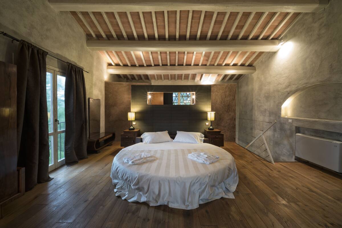 Quarto com uma cama grande, piso de madeira e teto inclinado com vigas aparentes.