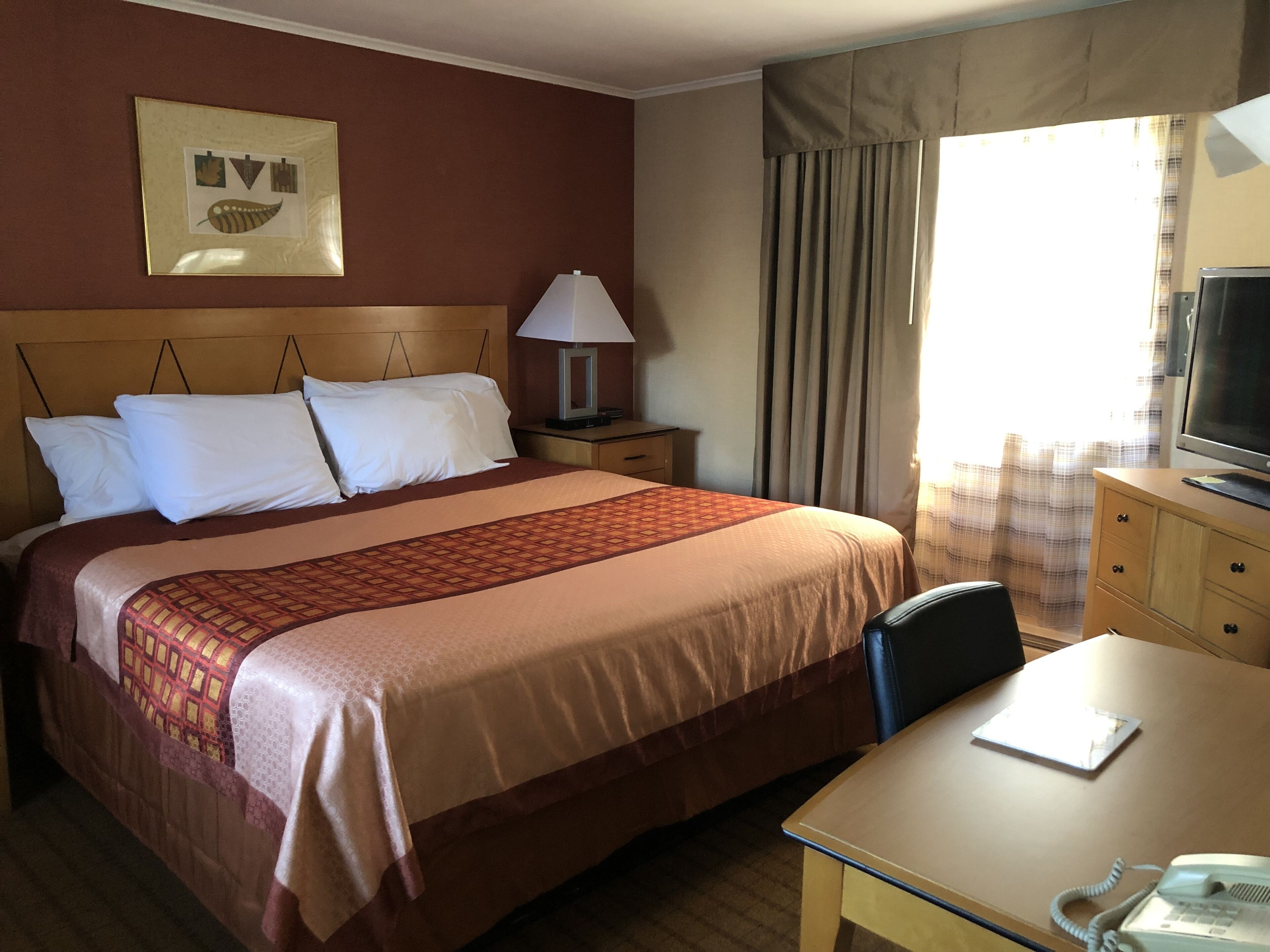 Quarto de hotel com cama, escrivaninha, cadeira, televisão e abajur.