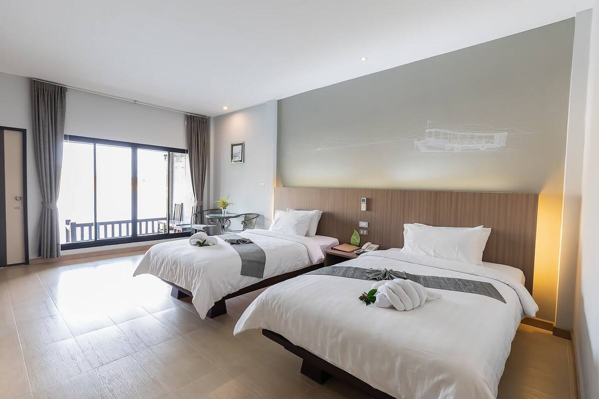 Quarto de hotel com duas camas, uma varanda e uma janela grande.