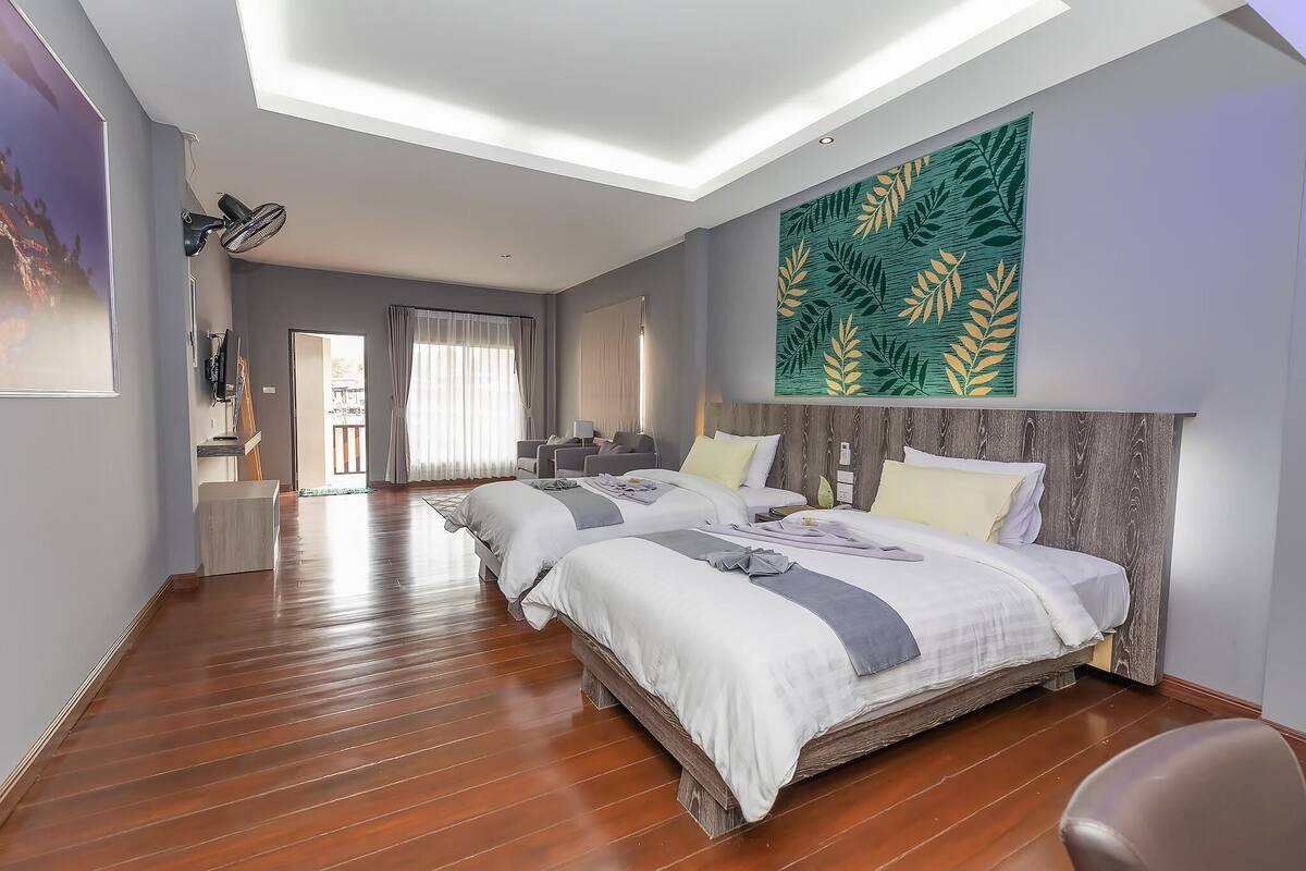 Quarto de hotel moderno com duas camas, uma janela grande e um ventilador de teto.