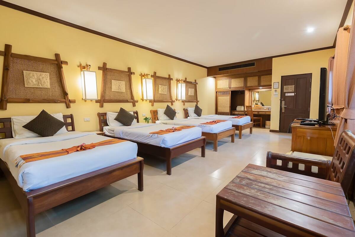 Quarto de hotel com três camas de madeira, uma escrivaninha de madeira e uma televisão.