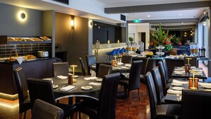 Restaurante com balcão central, diversas mesas de jantar com cadeiras e um buffet.