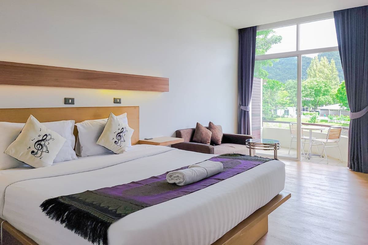 Quarto de hotel com uma cama grande, um sofá, uma mesa pequena e uma varanda com vista para o verde.
