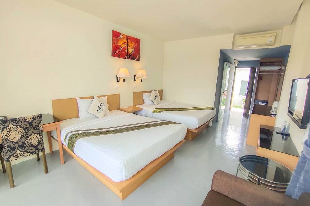 Quarto de hotel com duas camas, um sofá, uma televisão e um quadro na parede.