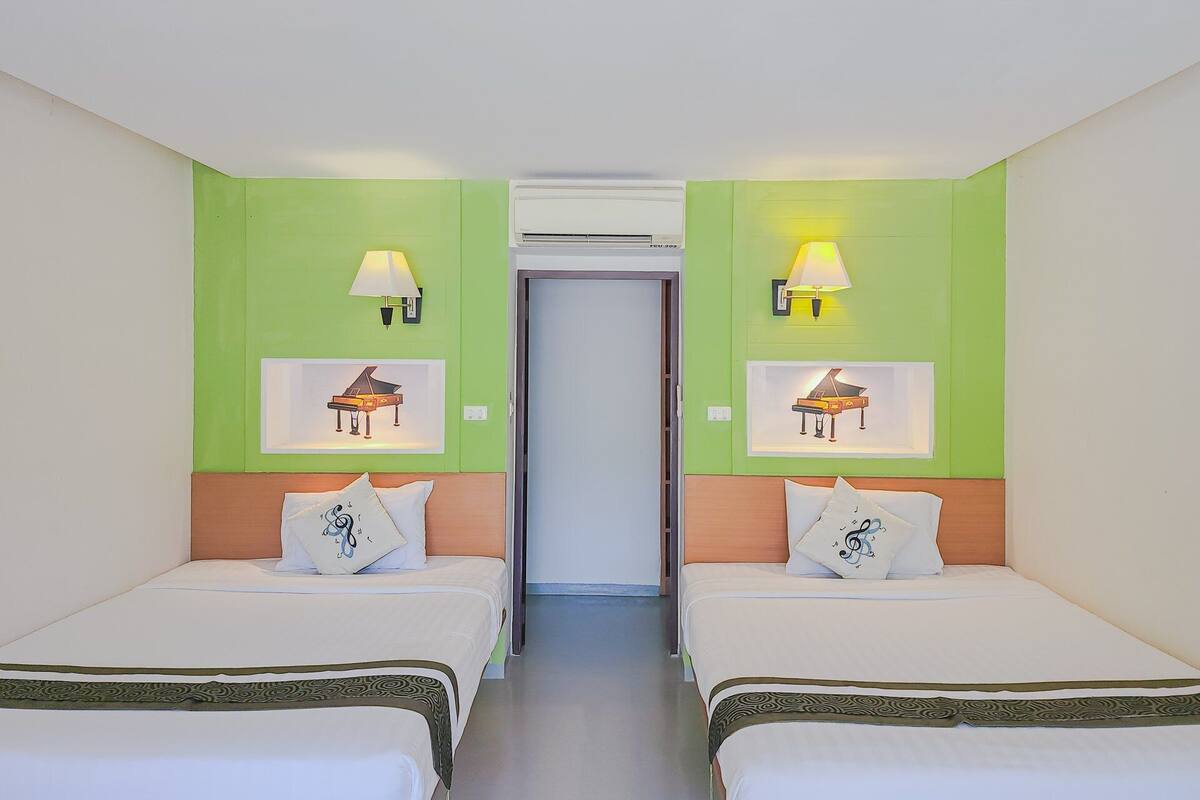 Quarto de hotel com duas camas de solteiro, paredes verdes e uma porta que dá para outro quarto.