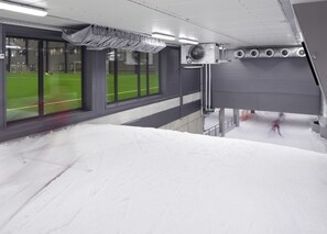 Um espaço interno coberto de neve, com janelas amplas, um ventilador e vista para um campo verde.