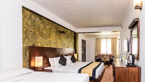 Quarto de hotel com duas camas, uma escrivaninha, uma cadeira, uma televisão e um banheiro visível por uma porta aberta.