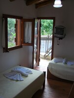 Quarto com duas camas, televisão e varanda com vista para o verde.