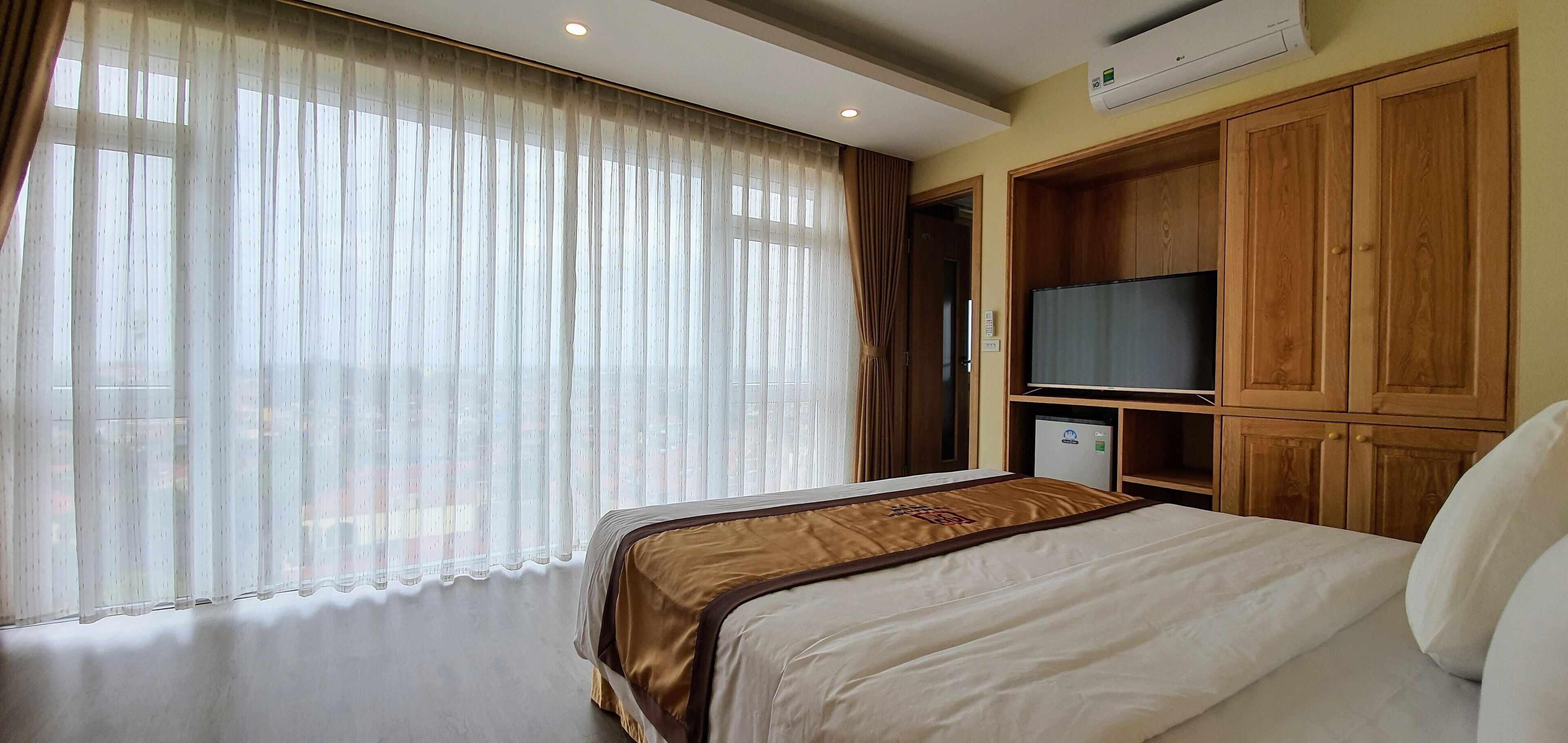 Quarto de hotel com cama, televisão, mini-frigorífico e armários de madeira.
