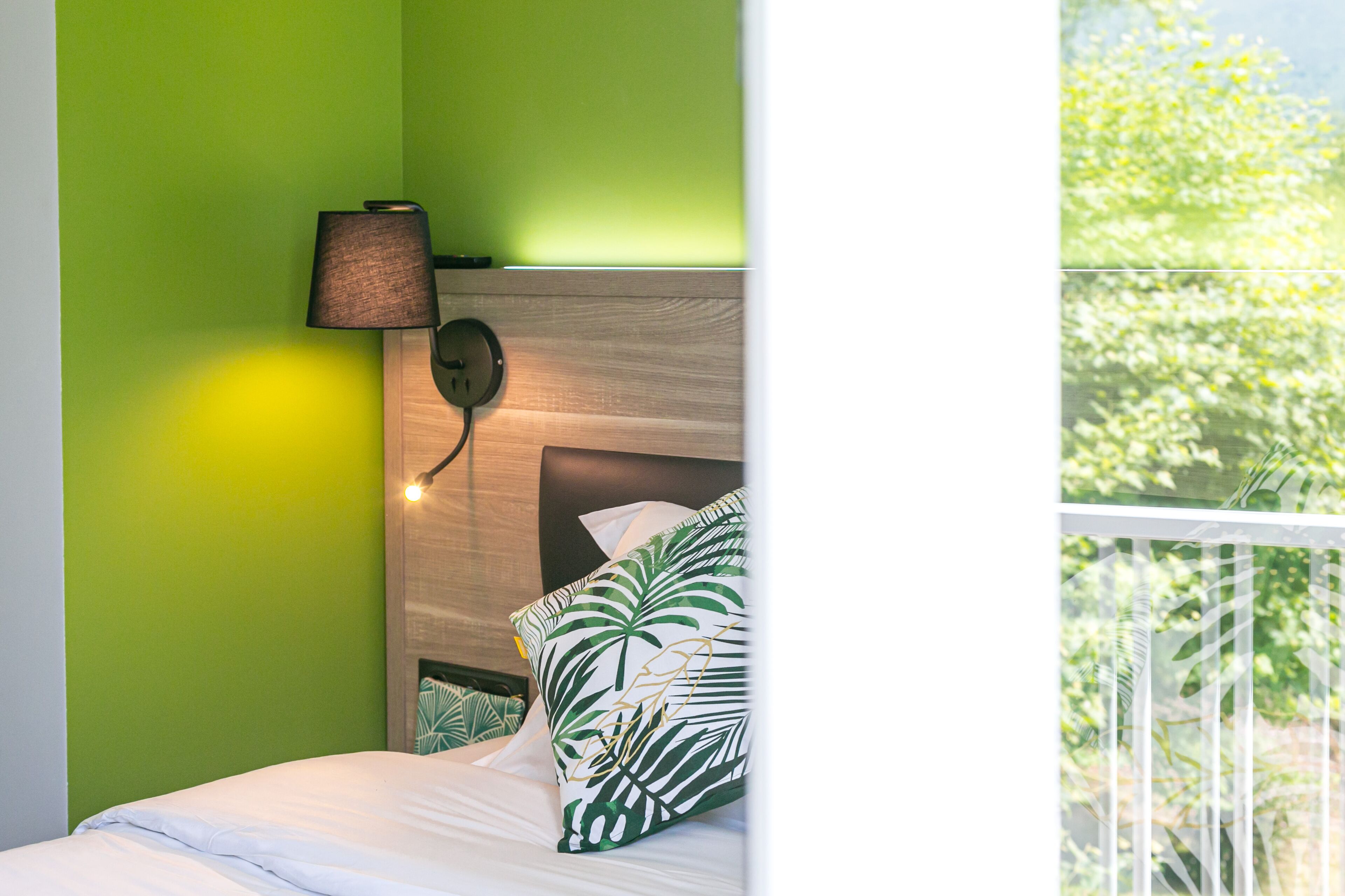 Uma cama com cabeceira de madeira, parede verde e janela com vista para árvores.